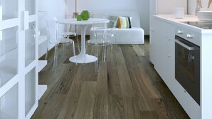 Uma cozinha moderna com armários brancos, uma área de refeições com cadeiras transparentes e um sofá com almofada colorida.