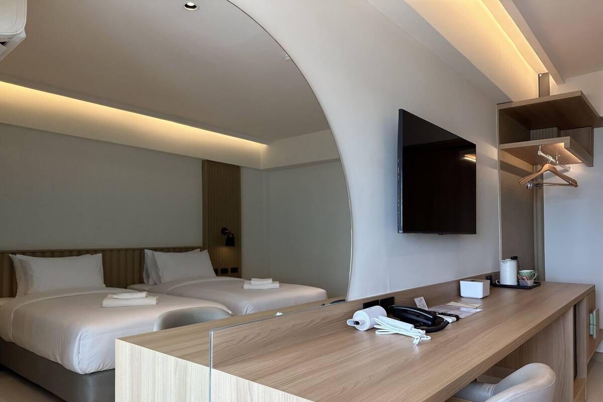 Quarto de hotel moderno com duas camas, uma escrivaninha com televisão de tela plana e um espaço para relaxar.