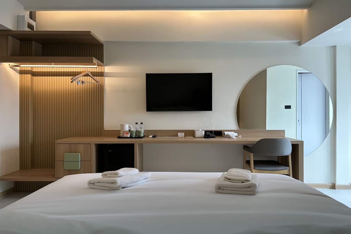 Quarto de hotel moderno com uma cama grande, uma escrivaninha com televisão de tela plana, um espelho e um guarda-roupa.