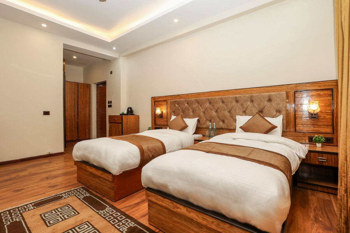 Quarto de hotel com duas camas, cabeceiras de madeira, mesas de cabeceira com luminárias e um tapete estampado.