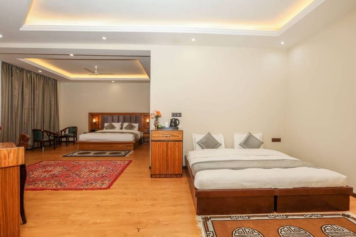 Quarto de hotel com duas camas, uma secretária de madeira, uma máquina de café e um tapete vermelho estampado.