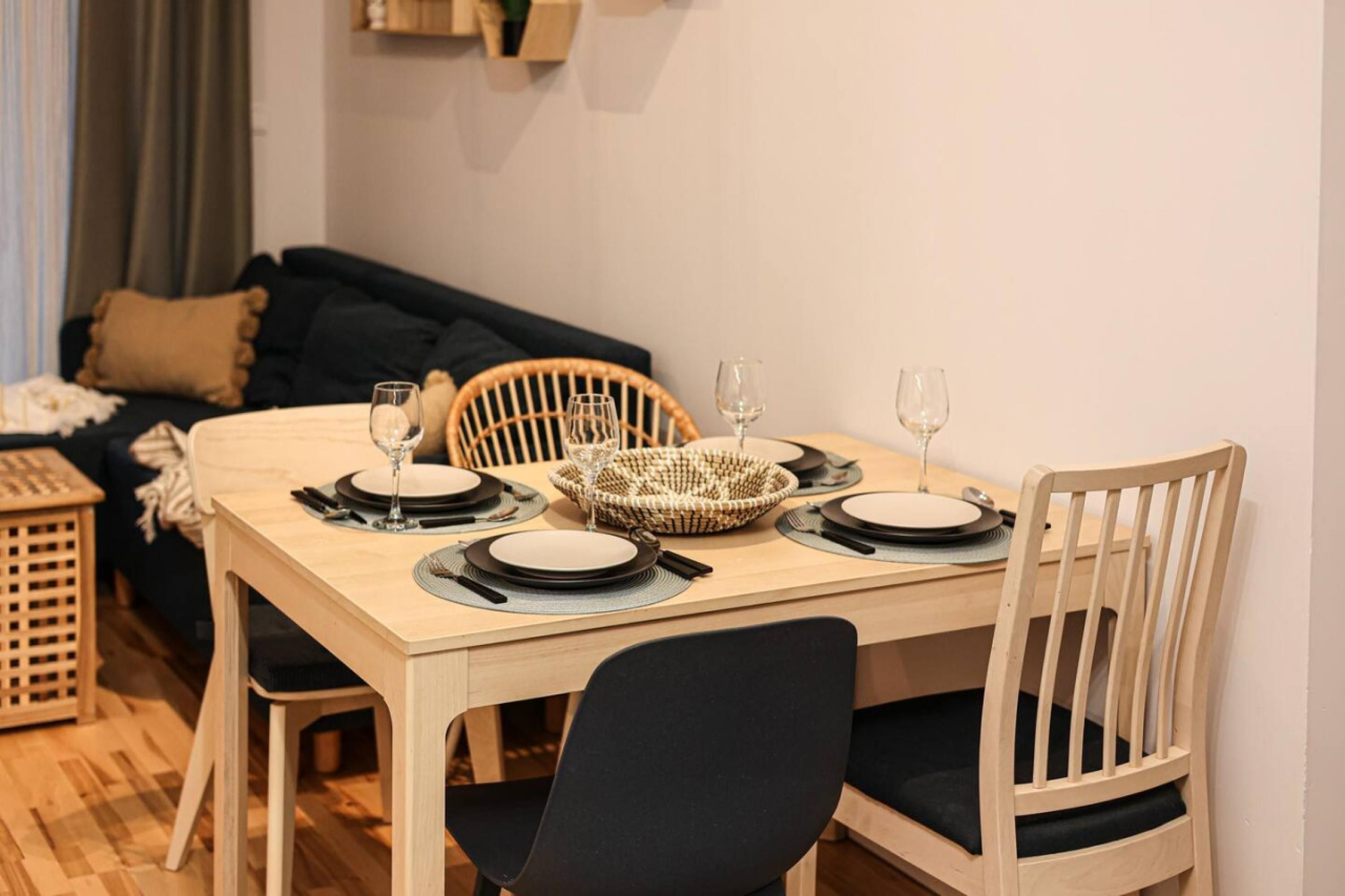 Mesa de jantar posta com pratos, talheres e copos, rodeada por cadeiras.