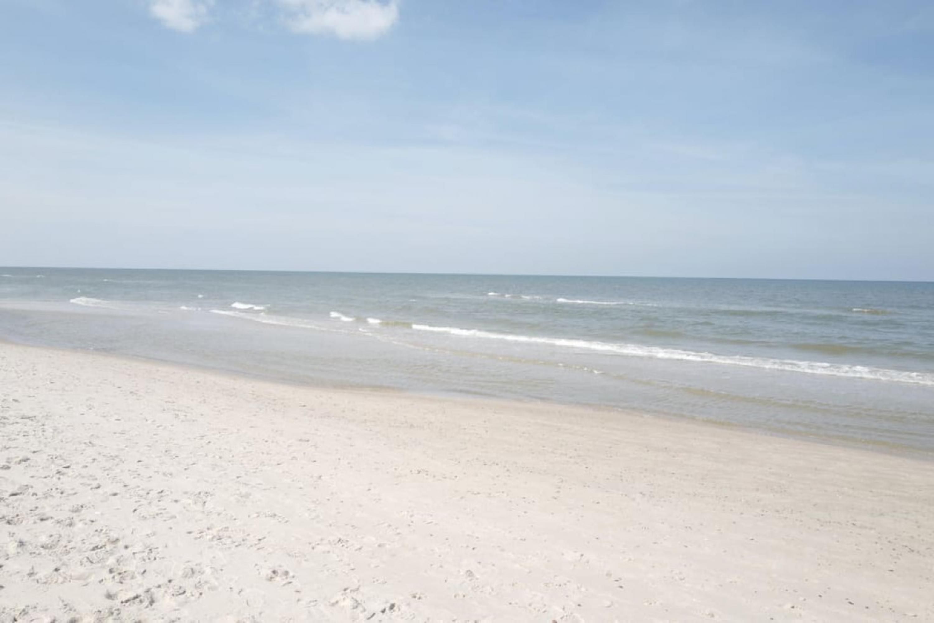Uma extensa praia de areia com ondas suaves e céu claro.
