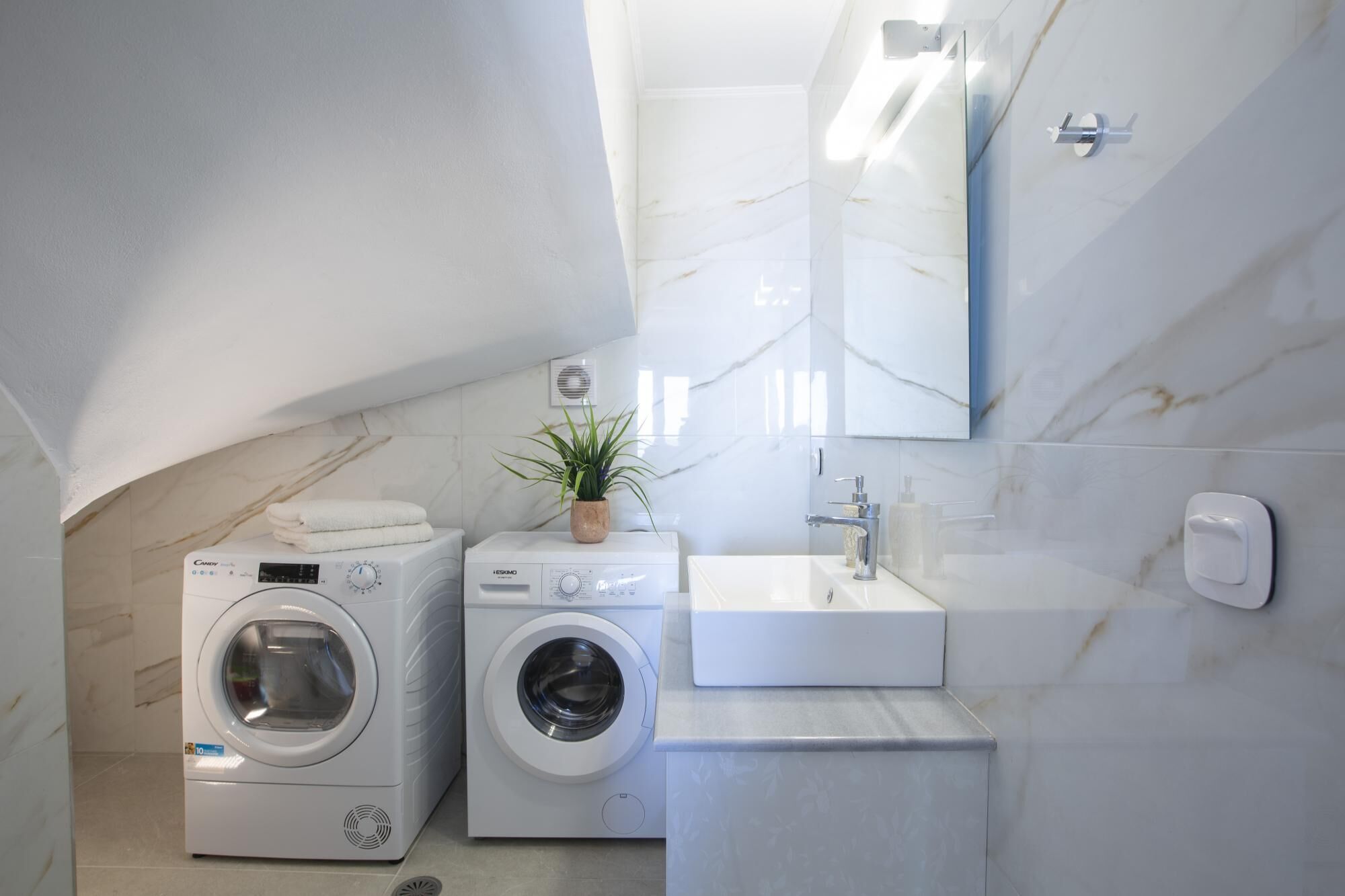 Casa de banho compacta e moderna com máquina de lavar e secar integradas, lavatório e espelho.