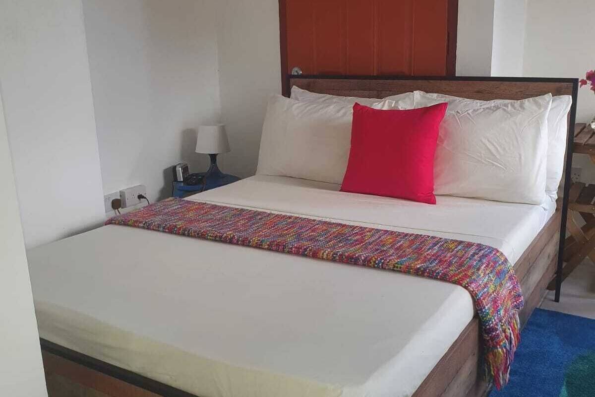Uma cama com estrutura de madeira, roupa de cama branca e um cobertor tecido colorido.