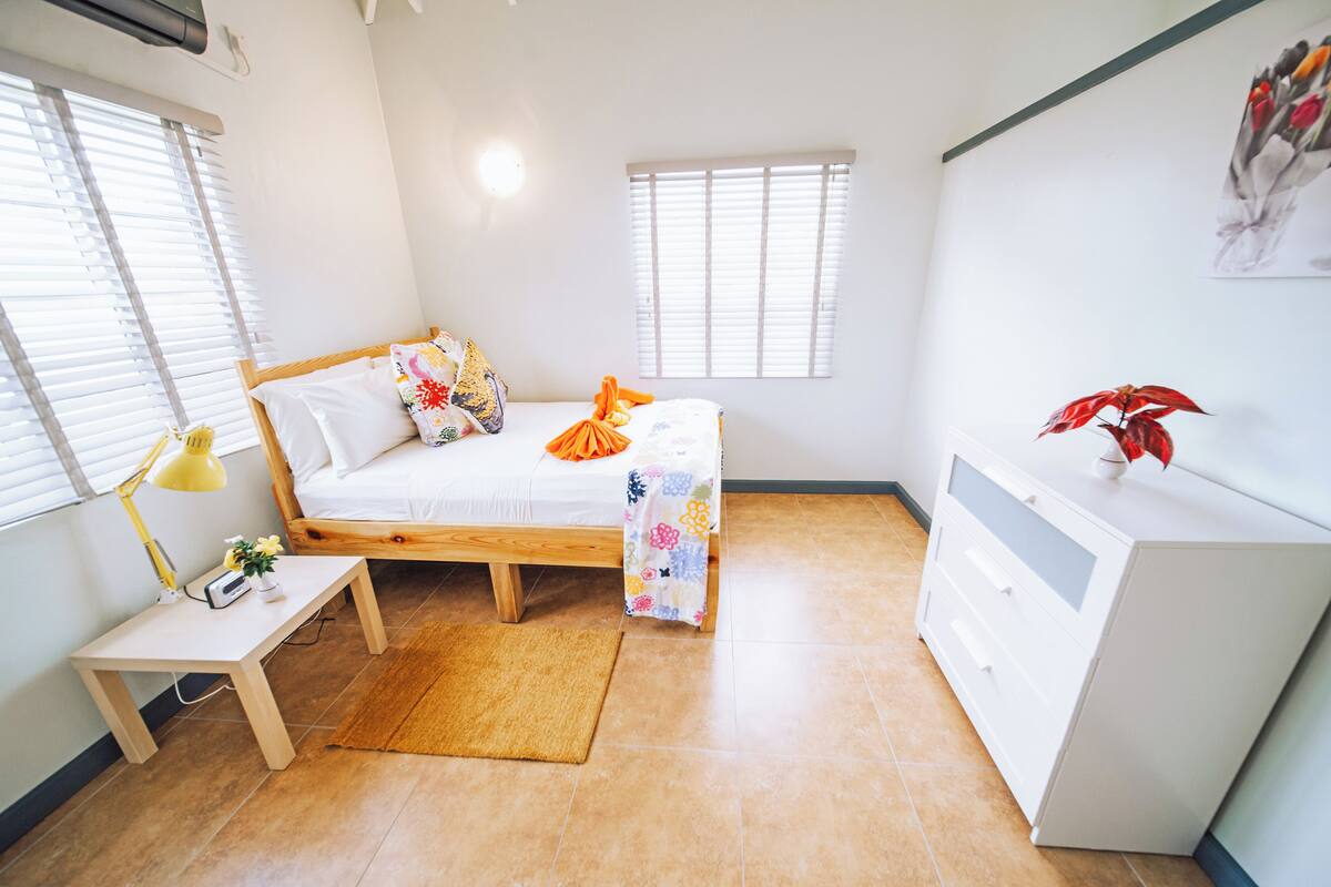 Quarto com cama, mesa de cabeceira, abajur e cômoda.