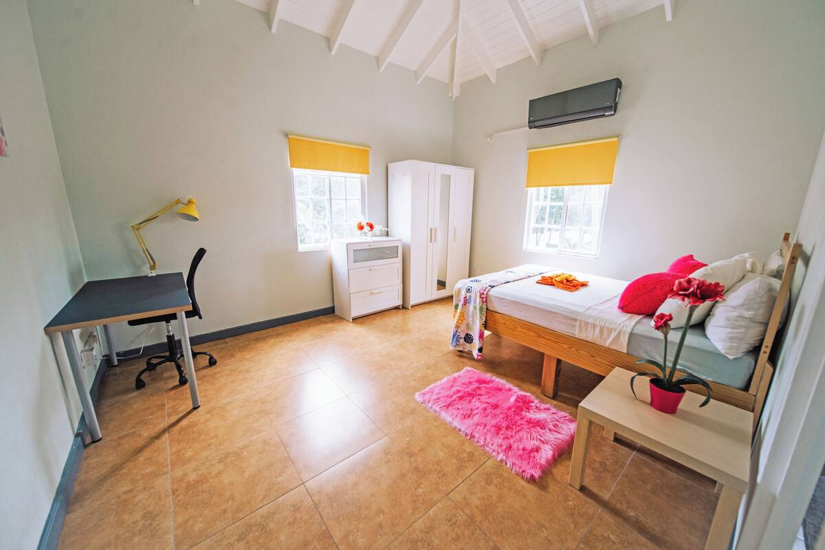 Quarto com cama, escrivaninha, cadeira, guarda-roupa e uma mesinha com uma planta.