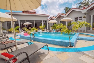 Área de piscina com espreguiçadeiras, guarda-sóis e uma cascata.