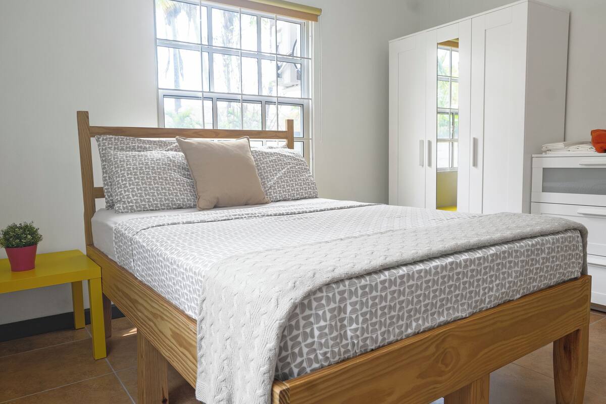 Quarto com cama, janela, guarda-roupa e uma pequena mesa com uma planta.
