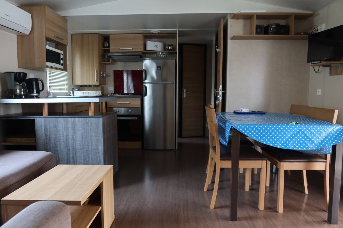 Cozinha compacta com micro-ondas, fogão e frigorífico. Dispõe de zona de refeições com mesa e cadeiras, e de kitchenette com armários e lava-loiça.
