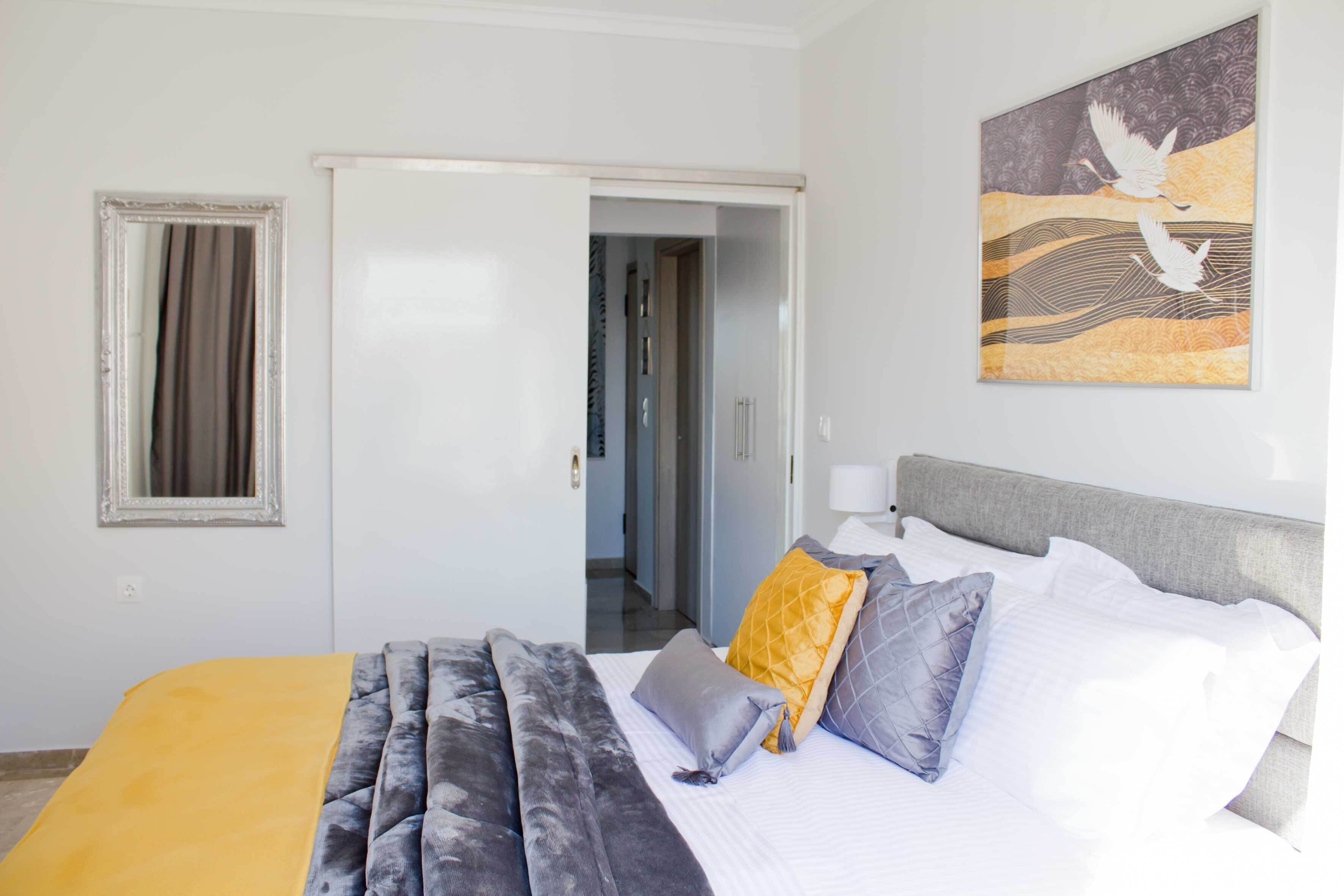 Quarto com cama, porta, espelho e um quadro na parede.