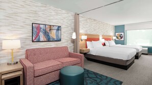 Quarto de hotel com cama, sofá, mesa de cabeceira, luminária e uma obra de arte na parede.