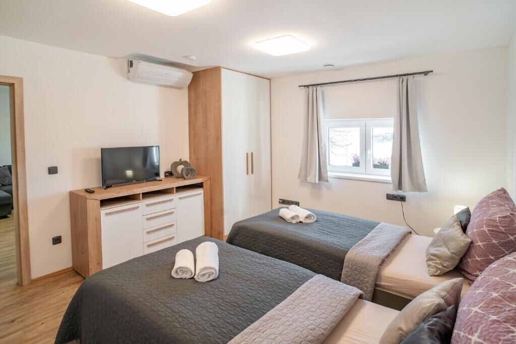 Quarto de hotel com duas camas, uma televisão, uma escrivaninha com gavetas e uma janela com cortinas.