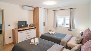 Quarto de hotel com duas camas, uma televisão, uma escrivaninha com gavetas e uma janela com cortinas.