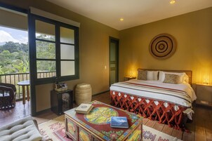 Um quarto com uma cama grande, uma mesa pequena com livros, um objeto decorativo e vista para o exterior.