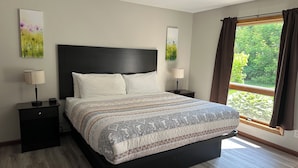 Quarto com uma cama grande, duas mesas de cabeceira com abajures, uma cabeceira e duas pinturas penduradas na parede.
