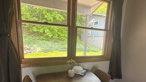 Um quarto com uma mesa de madeira redonda, duas cadeiras, um vaso com flores e uma janela com cortinas.