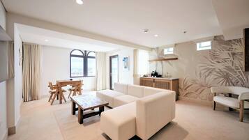 Uma sala de estar moderna com um sofá, uma mesa de centro, área de jantar com cadeiras, cozinha com bancada e uma grande janela.