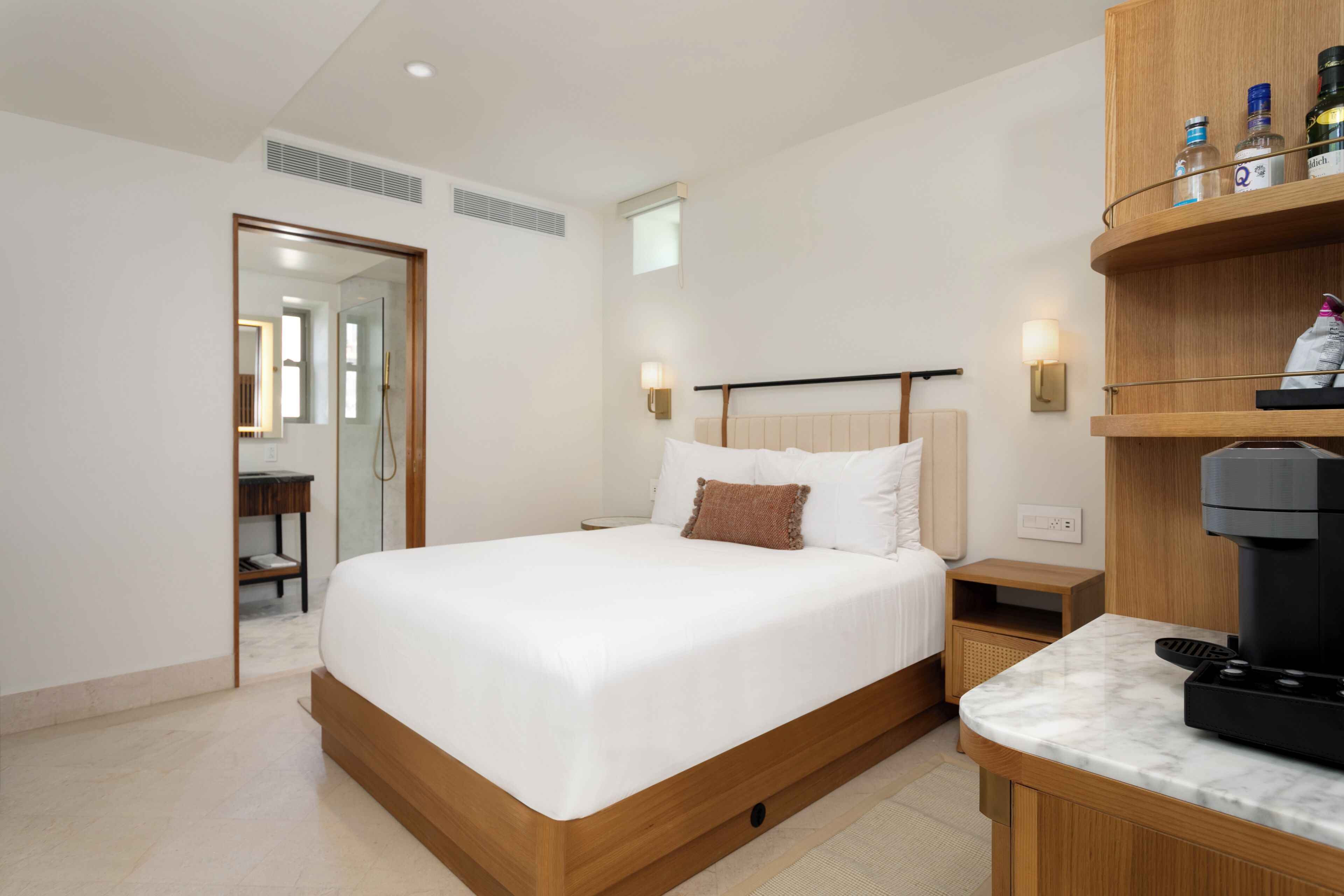 Quarto de hotel com cama, mesas de cabeceira, máquina de café embutida e um espelho.