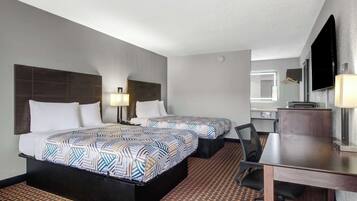 Quarto de hotel com duas camas, uma escrivaninha, uma cadeira, uma televisão e um espelho.