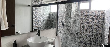 Casa de banho moderna com um espelho grande, lavatório suspenso, sanita e área de duche com azulejos estampados.