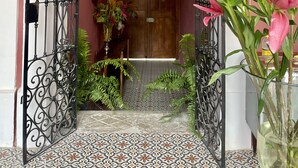 Uma entrada tradicional com um portão de metal decorativo, uma porta de madeira e piso de azulejos.