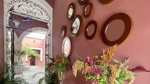 Um corredor com chão de azulejos estampados, um console de madeira com vasos e uma série de espelhos na parede.