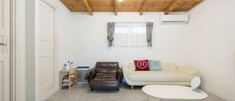 Um quarto com teto de madeira, uma poltrona de couro, um sofá, uma mesa pequena e uma janela com cortinas.