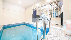 Uma piscina interna com azulejos azuis vibrantes, uma escada de metal e piso revestido de azulejos.