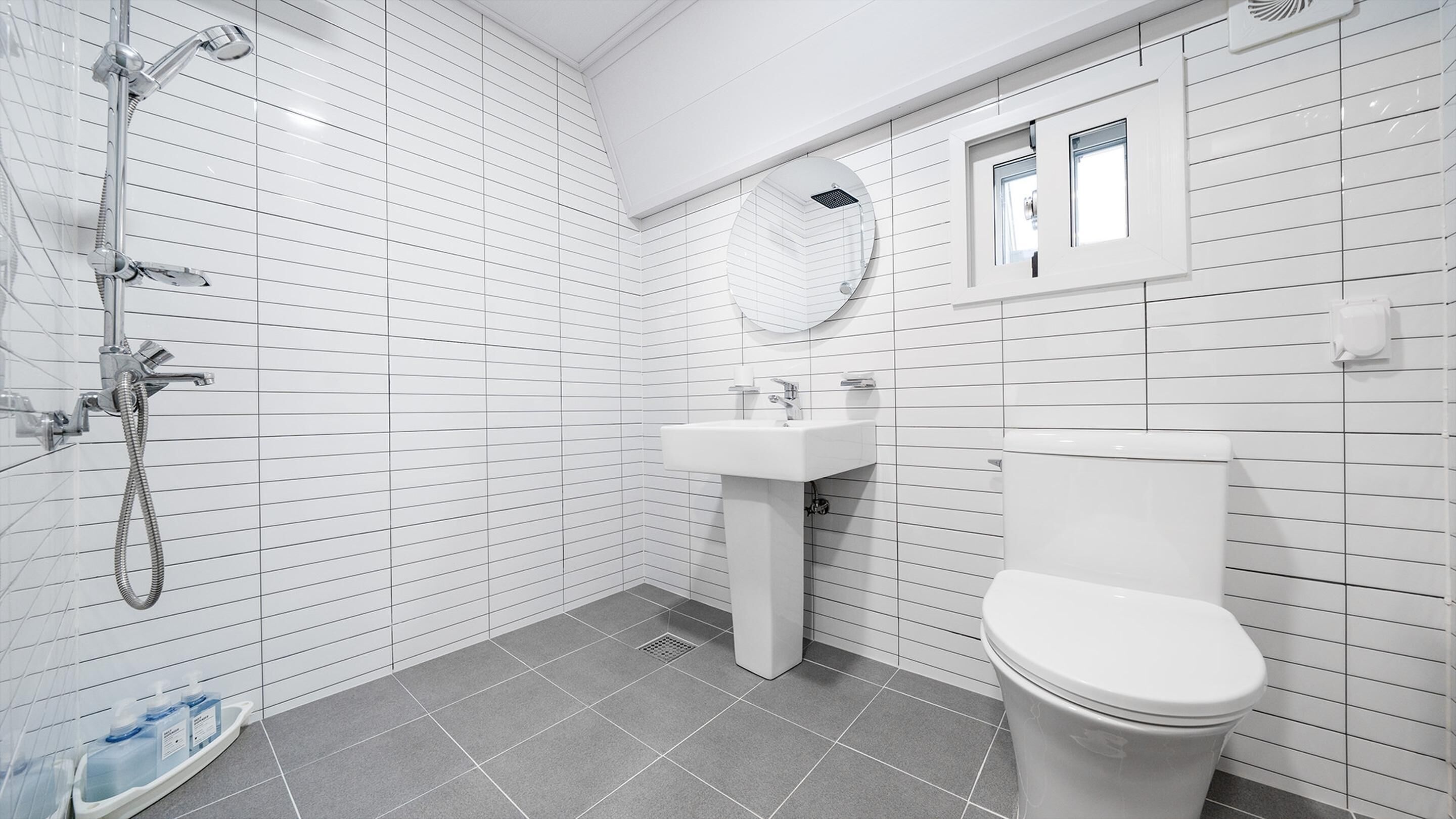 Um banheiro moderno com azulejos brancos tipo metrô, pia branca, vaso sanitário e chuveiro com chuveiro manual.