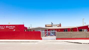 Um prédio vermelho com entrada gradeada, uma placa com a inscrição 'China's Guesthouse' e um céu azul claro.