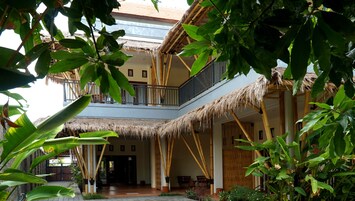 Um edifício de dois andares com telhado de palha, pilares de bambu e uma varanda com grade.
