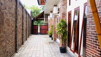 Um corredor de tijolos estreito, com chão de azulejos, plantas em vasos e um portão de madeira.