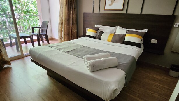 Quarto moderno com uma cama grande, uma varanda com uma cadeira e vista para o verde.
