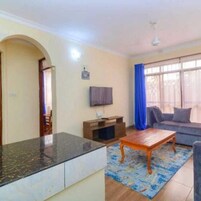 Uma sala de estar com sofá, mesa de centro e TV fixada na parede.