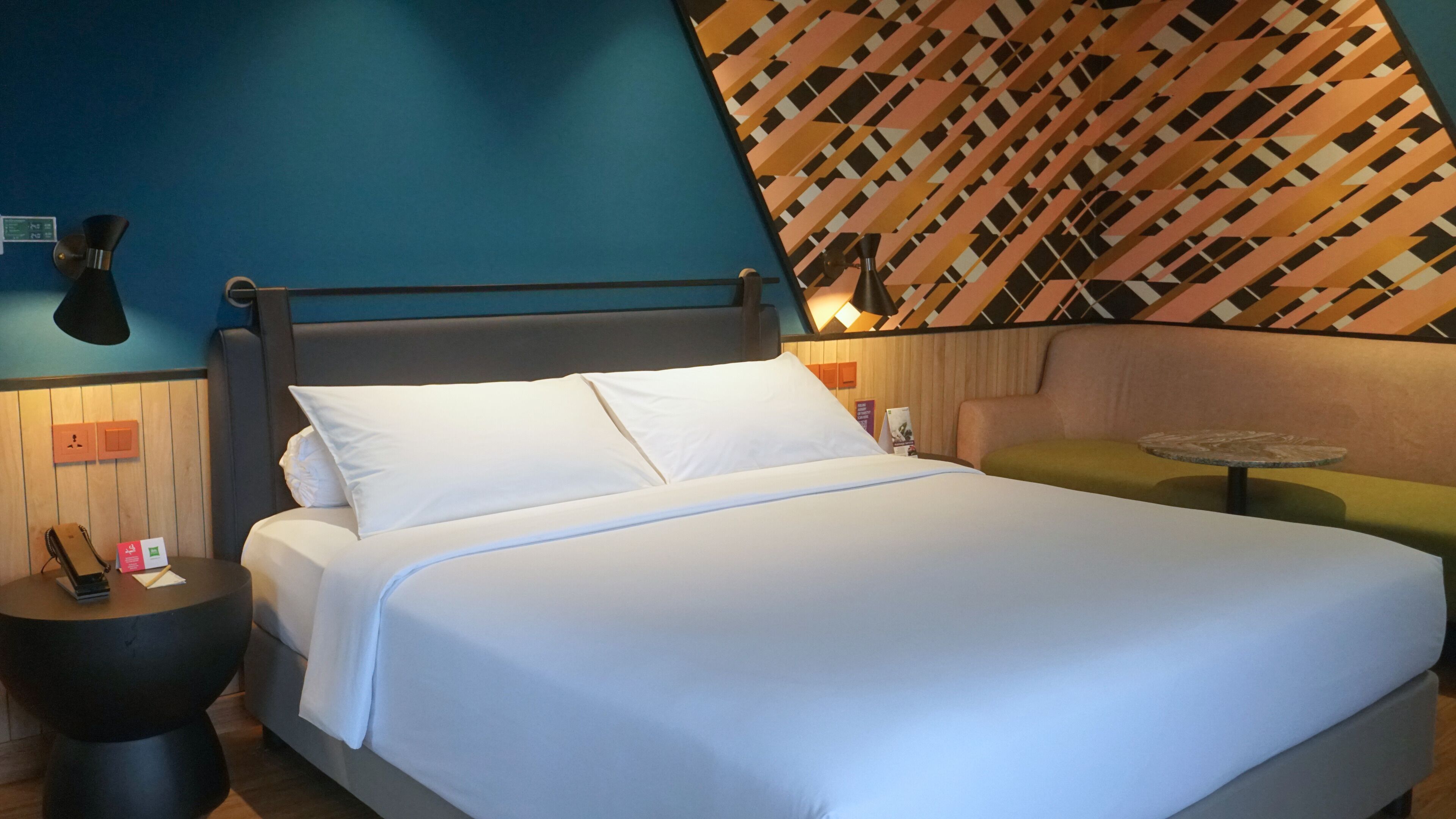 Quarto de hotel moderno com uma cama grande, uma mesa redonda e um design de parede geométrico único.