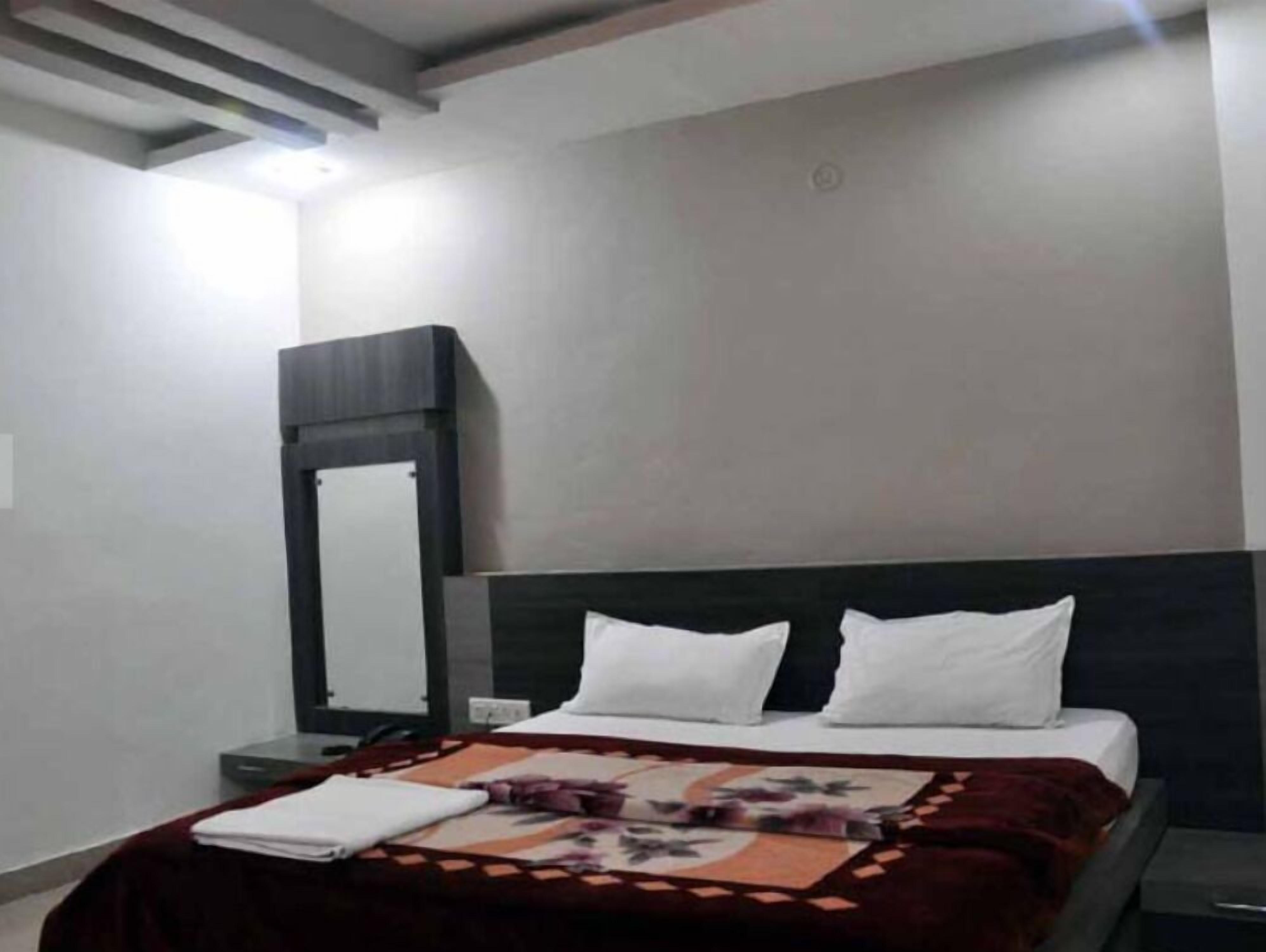 Quarto de hotel com cama, mesa de cabeceira, espelho e luminária na parede.