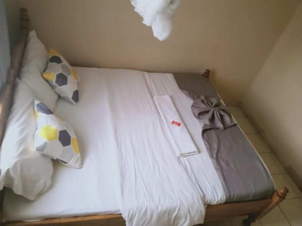 Uma cama com lençol branco, manta cinza e travesseiro com padrão geométrico.