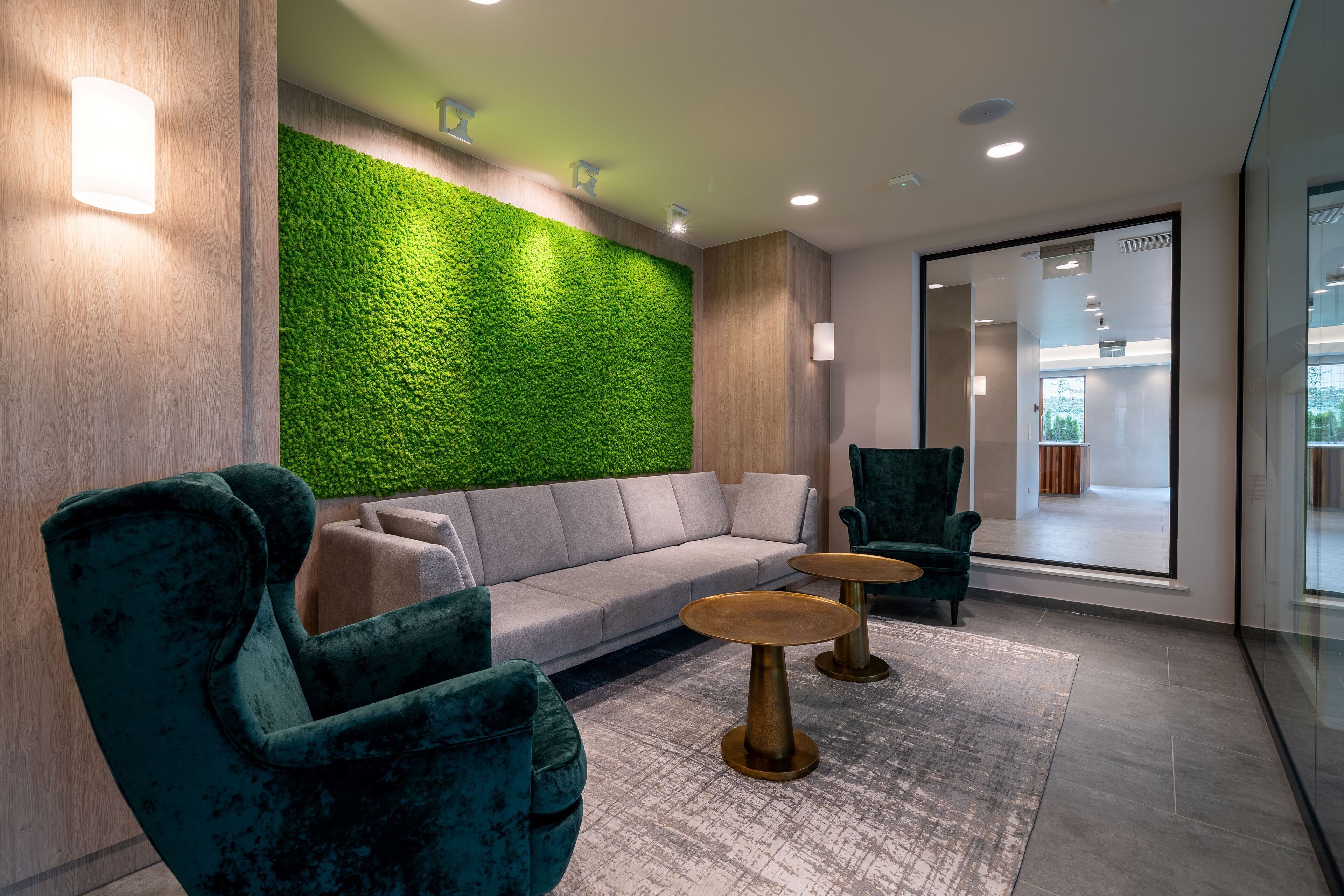 Um hall moderno com parede verde, sofá cinzento, poltronas azul-esverdeadas e uma mesa de centro.