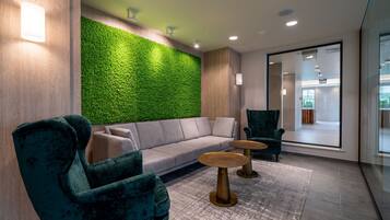 Um hall moderno com parede verde, sofá cinzento, poltronas azul-esverdeadas e uma mesa de centro.