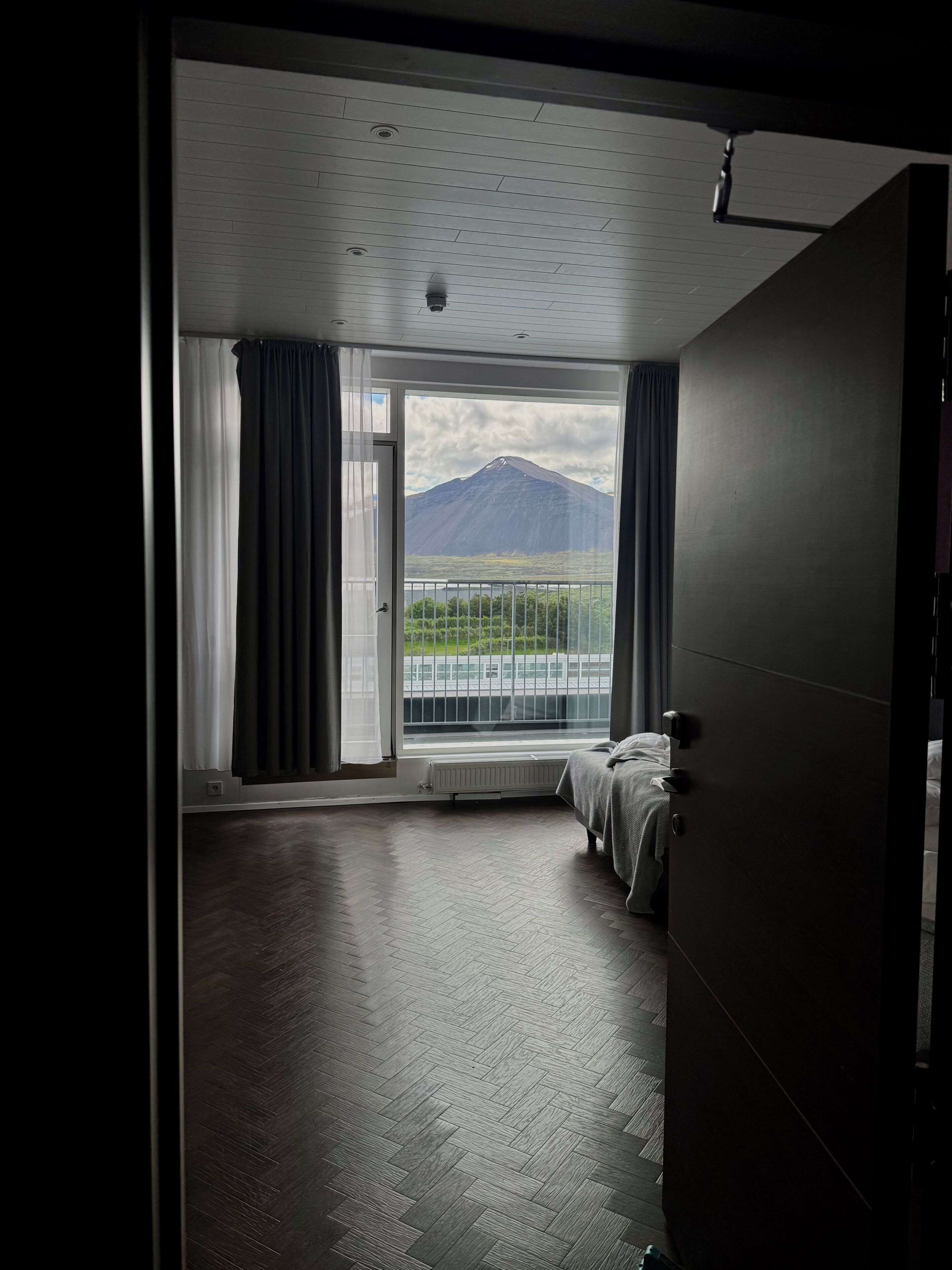 Quarto de hotel com cama, radiador e vista para uma montanha através de uma janela.