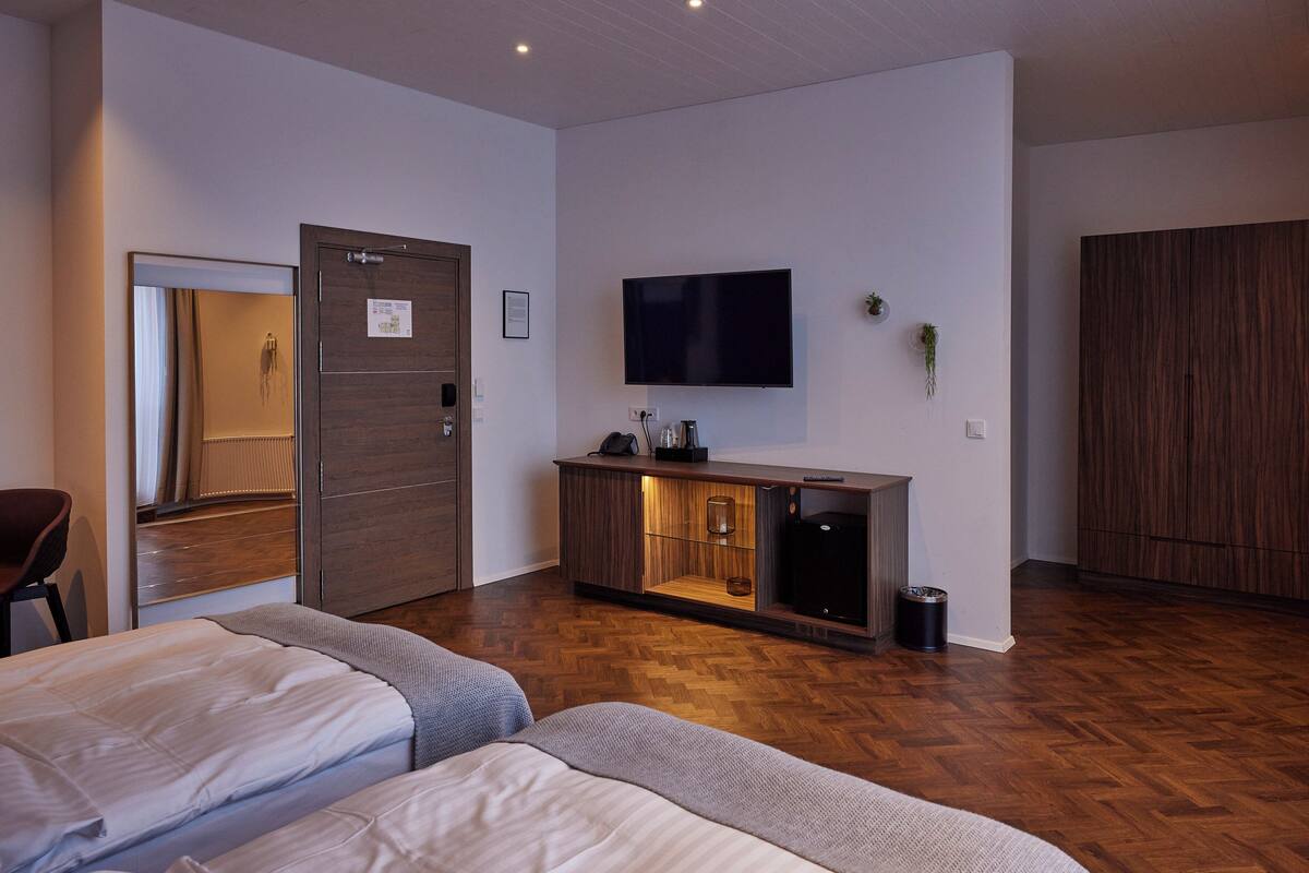 Quarto de hotel com duas camas, uma televisão, um armário de madeira e uma porta para o banheiro.