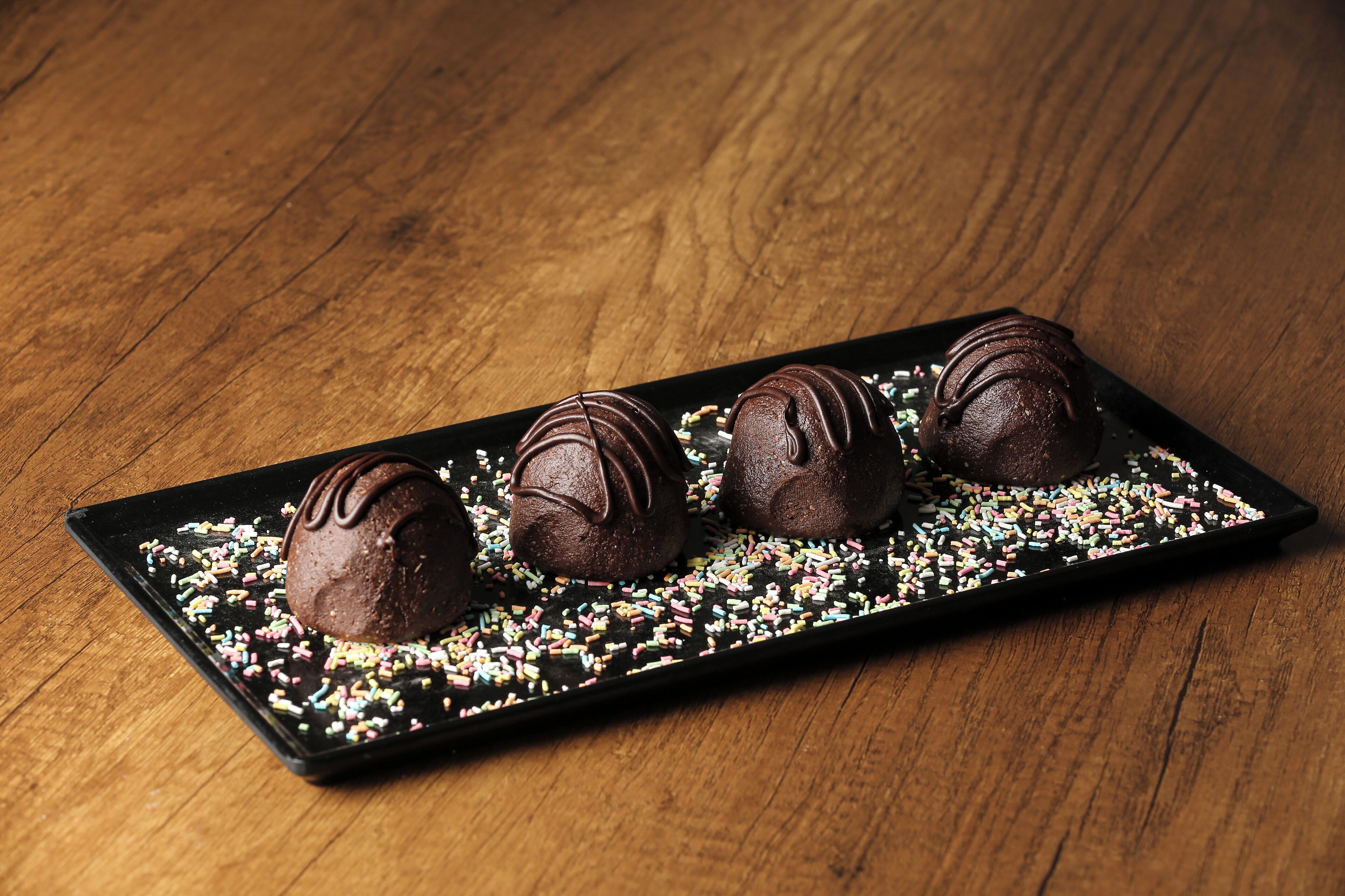 Uma sobremesa de chocolate em um prato preto com confeitos coloridos.