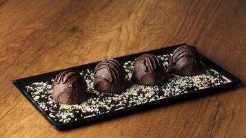 Uma sobremesa de chocolate em um prato preto com confeitos coloridos.