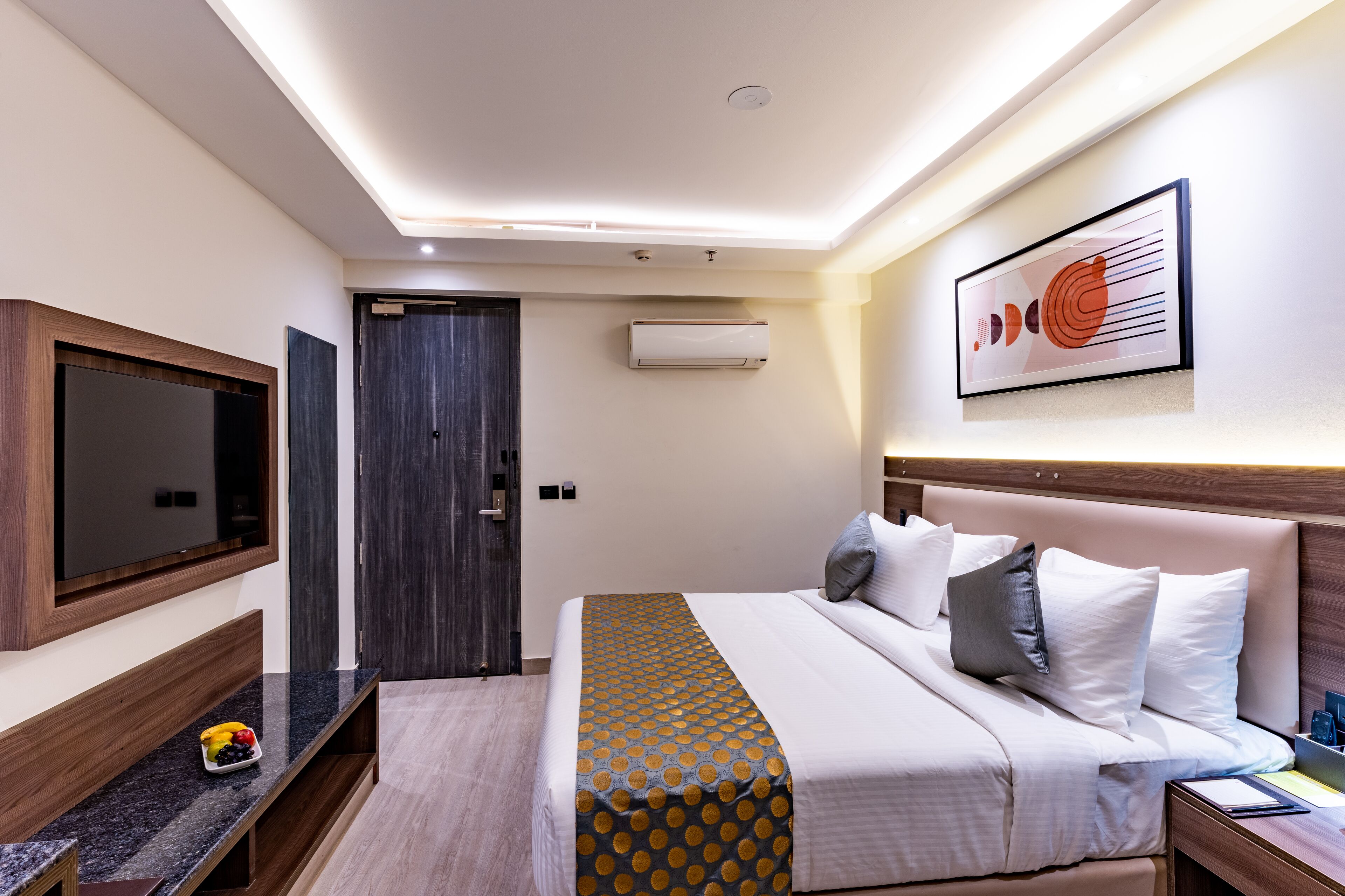 Quarto de hotel com cama, televisão, secretária e uma cesta de frutas.