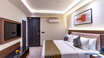 Quarto de hotel com cama, televisão, secretária e uma cesta de frutas.