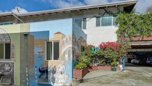 Uma casa de dois andares com um mural lateral, uma garagem e uma árvore com flores cor-de-rosa.