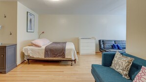 Quarto com cama, cômoda, mesa de cabeceira, sofá e luminária no teto.