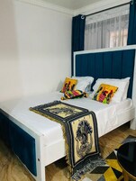 Uma cama com colchão branco, cabeceira azul e almofadas coloridas.