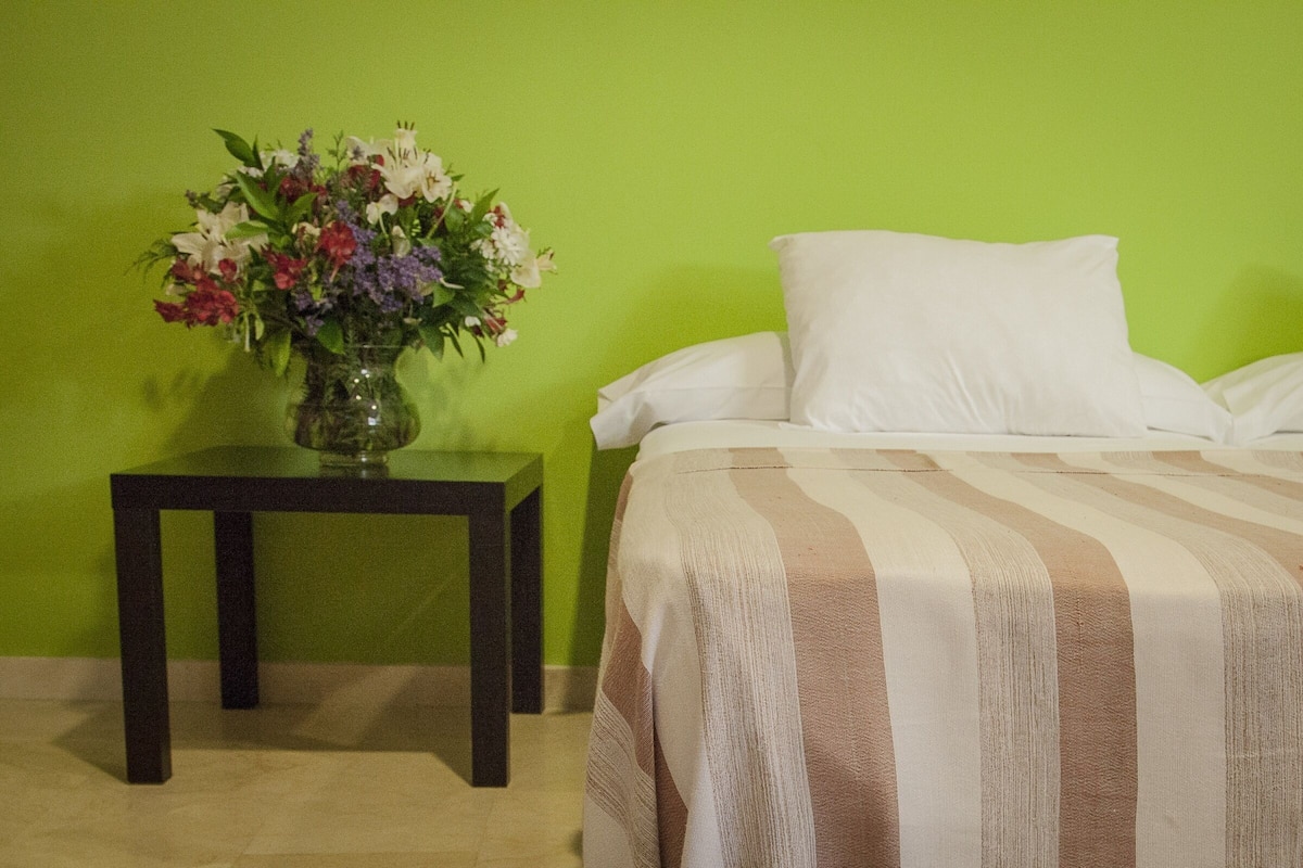 Um quarto com uma cama, uma mesa de cabeceira e um vaso de flores.